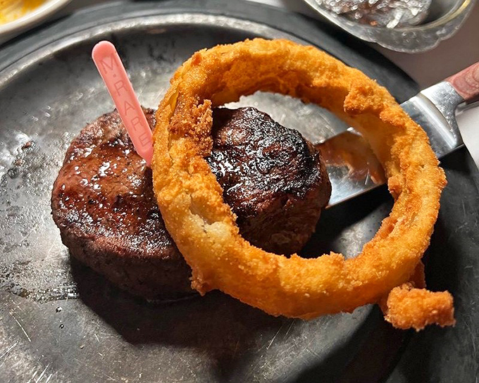 A perfectly seared filet mignon crowned with a golden onion ring—like a tiny edible Saturn orbiting your plate of beefy perfection.