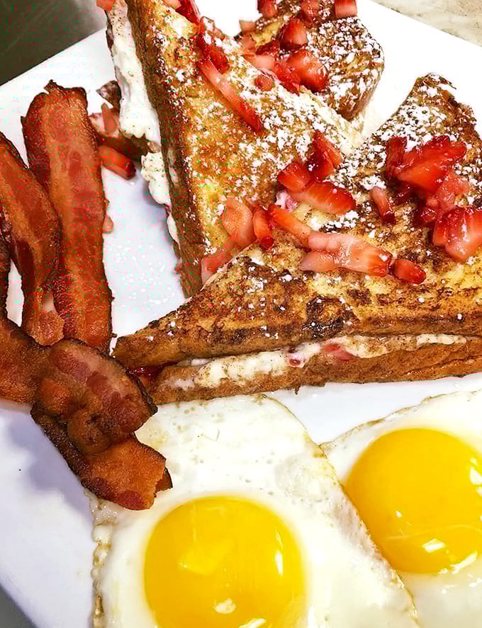 French toast that's dressed for success with fresh strawberries, powdered sugar, and a side of bacon that's living its best life.