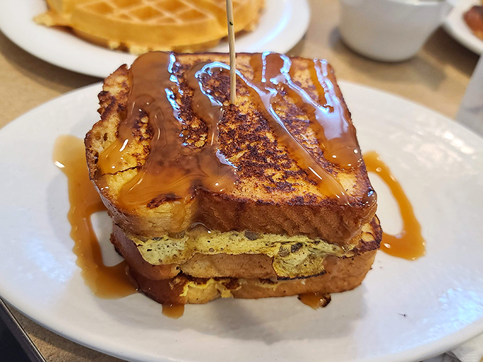 French toast elevated to art form, drizzled with syrup that cascades like liquid gold across crispy perfection.