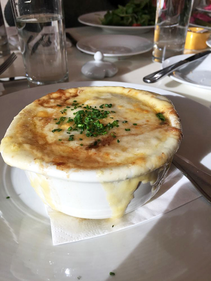 The legendary French onion soup arrives with cheese cascading down the sides like a dairy waterfall. Resistance is futile.