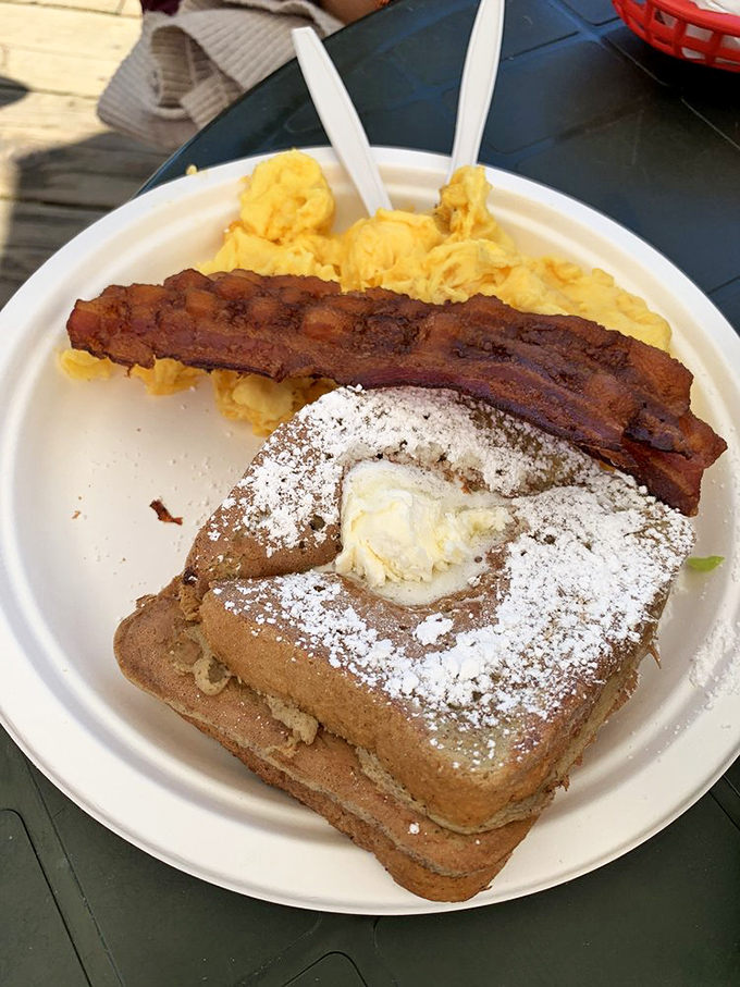 French toast that's dressed for success with powdered sugar, a pat of butter, and a strip of bacon standing guard like it knows something we don't.