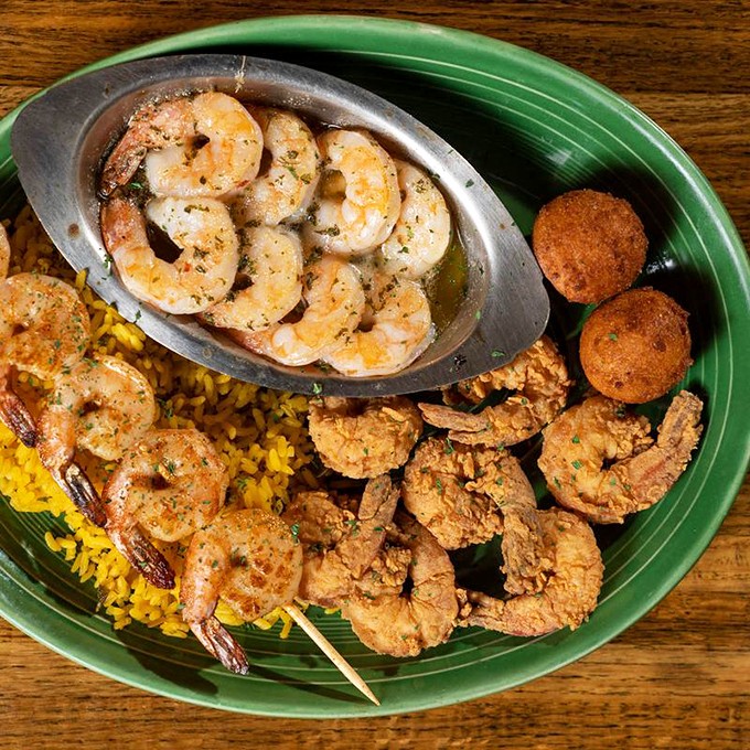 The holy trinity of seafood perfection: grilled, fried, and scampi-style shrimp sharing a plate with those legendary hush puppies and sunny yellow rice.