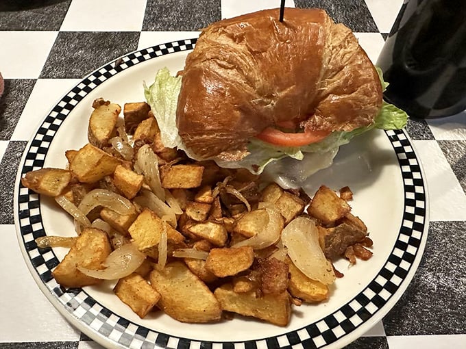 A croissant sandwich surrounded by golden home fries that look like they've been practicing their crispy-on-the-outside, fluffy-inside routine for decades.