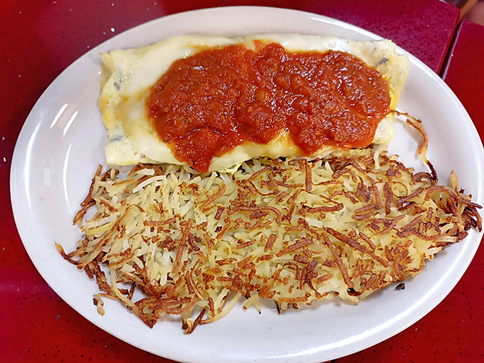 This omelet doesn't just sit on the plate—it commands attention with its blanket of sauce and perfectly crisp hash browns.