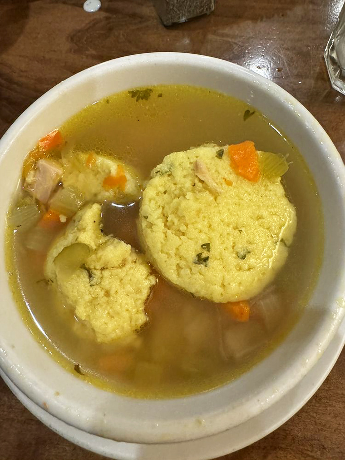 Fluffy matzo balls float like clouds in a golden sea of broth—chicken soup that could cure anything from colds to existential crises.