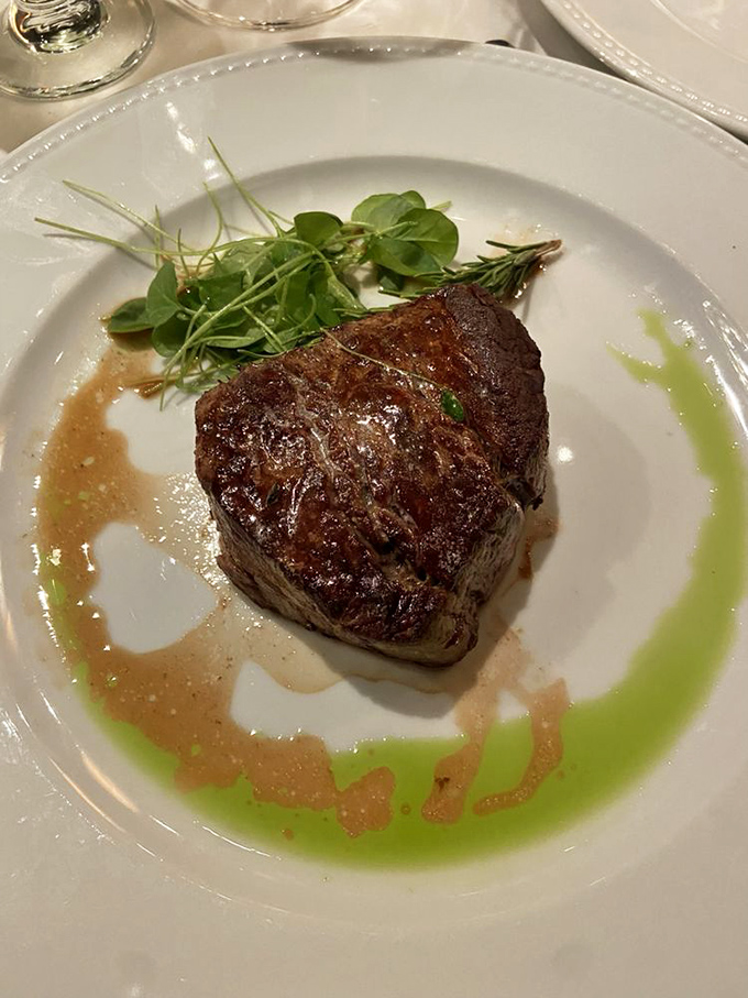 The filet mignon arrives like culinary royalty on its pristine throne, surrounded by artistic sauce flourishes that are almost too beautiful to disturb.