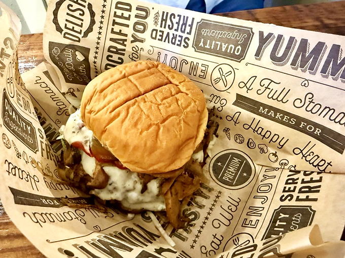 The Mushroom Swiss burger arrives nestled in branded paper, the creamy sauce and earthy mushrooms creating a symphony of flavors that Mozart would envy.