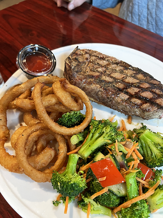 A perfectly grilled NY Strip with crispy onion rings and vibrant vegetables—proof that sometimes the classics become classics for very good reasons.
