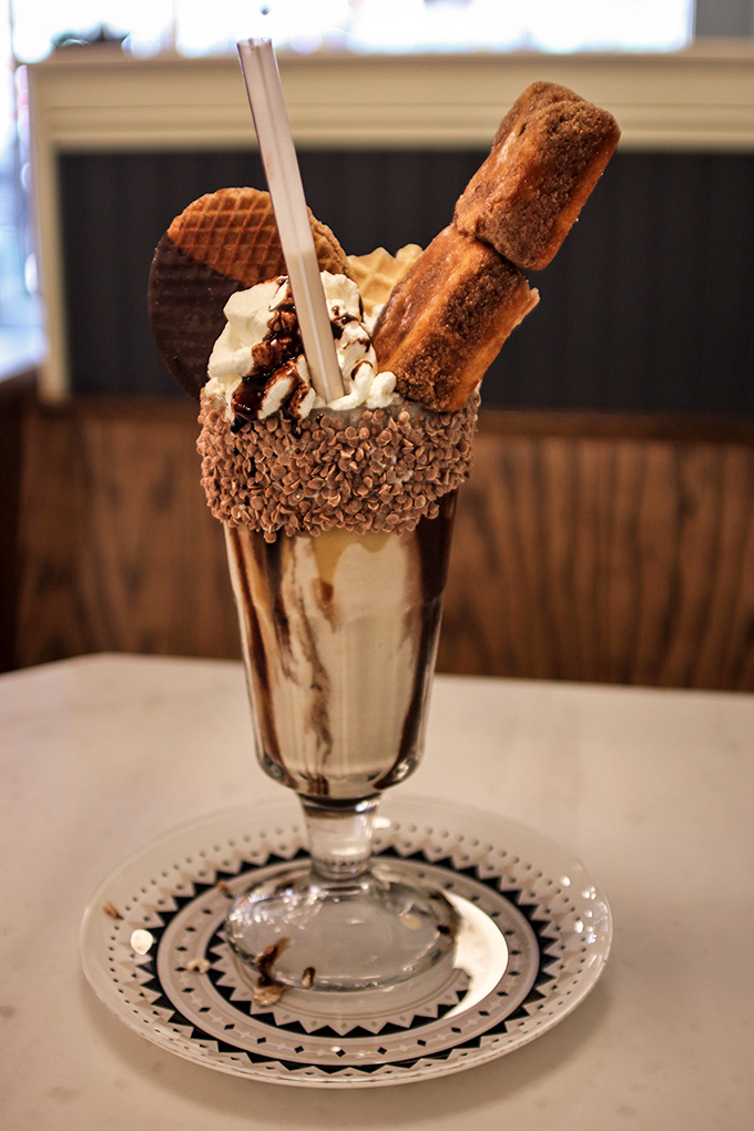 This isn't just a milkshake&mdash;it's an architectural marvel with chocolate, waffle pieces, and what appears to be churros standing guard over creamy perfection.