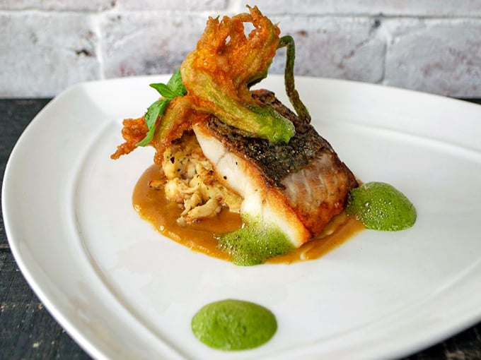 This isn't just fish &ndash; it's an artistic statement. Crispy-skinned bass perches atop a vibrant medley, garnished with a tempura-fried squash blossom.