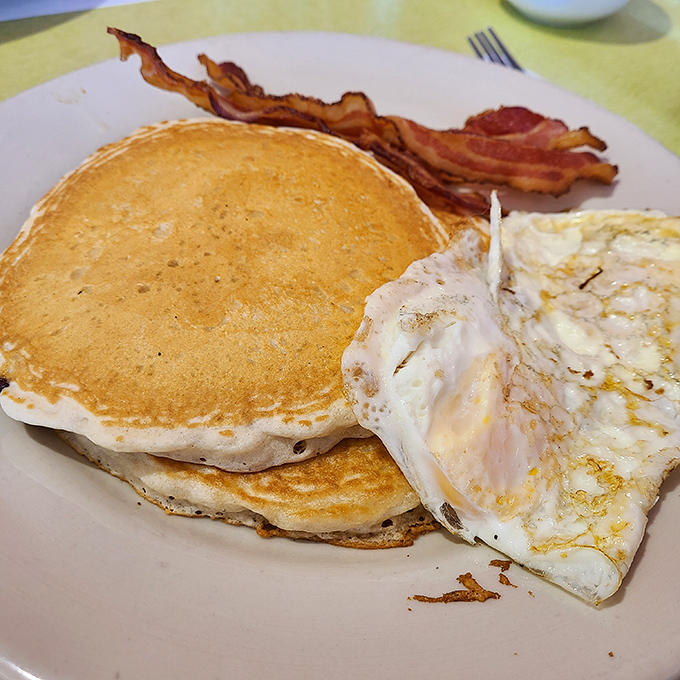 Pancakes so perfectly golden they belong in Fort Knox, paired with eggs and bacon that would make any breakfast purist weep with joy.