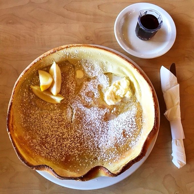 The German pancake arrives like edible architecture&mdash;a golden crater of deliciousness dusted with powdered sugar and awaiting its lemon squeeze destiny.