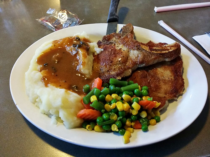 Comfort food personified: golden pork chops nestled against cloud-like mashed potatoes, with gravy that doesn't know the meaning of moderation.