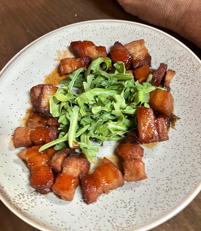 Thick-cut pork belly that transforms humble bacon into something approaching fine art with maple syrup glaze and fresh greens.