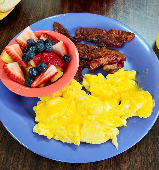 Sunshine on a plate: Fluffy scrambled eggs, crispy bacon, and a rainbow of fresh fruit. The breakfast equivalent of hitting every green light on your morning commute.