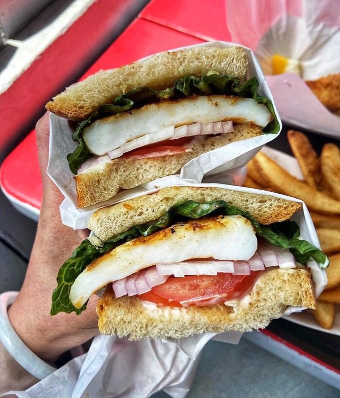 A fish sandwich that makes bread feel privileged. Fresh greens, ripe tomato, and perfectly grilled seafood &ndash; the holy trinity of sandwich perfection.