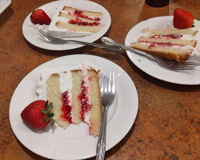 Three slices of strawberry shortcake heaven await, each layer telling a story of sweet berries, light cake, and cream that defies gravity.