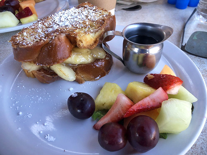 French toast that's clearly been to finishing school. The powdered sugar snowfall and fresh fruit side make breakfast feel like a special occasion.