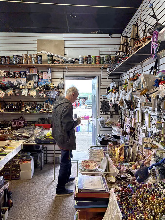 A treasure hunter examines wares in a booth packed floor-to-ceiling with collectibles. One person's clutter becomes another's prized possession.