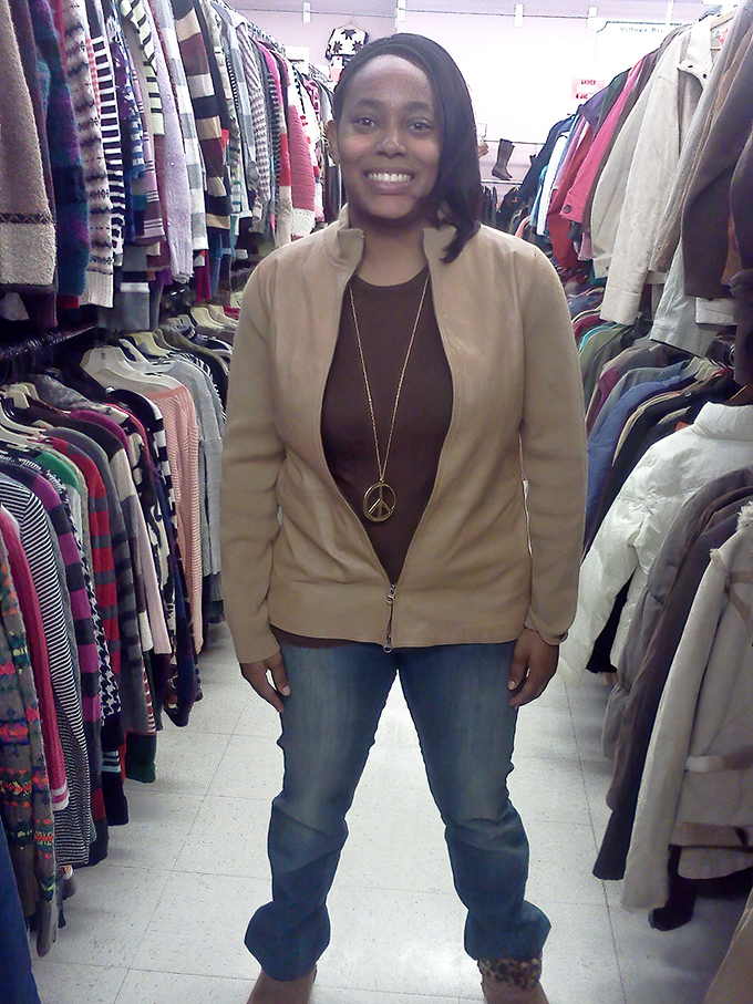 The image shows a shopper standing among clothing racks, demonstrating how Village Discount Outlet offers something for everyone's personal style journey.