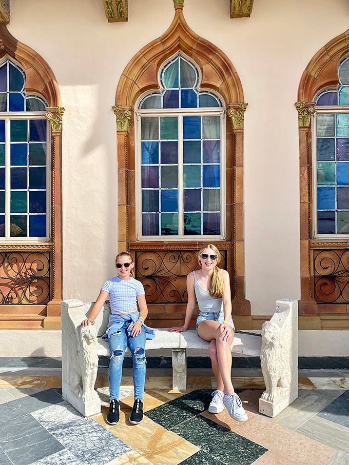 Stained glass windows frame visitors enjoying a moment of repose, their colorful patterns casting jewel-toned light across the mansion's marble benches.