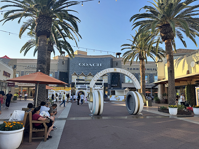 Palm trees frame the Coach store's impressive entrance, where shoppers gather like pilgrims at a temple dedicated to discounted leather goods.