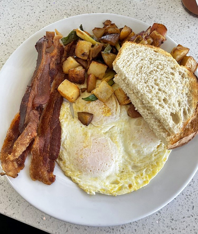 The breakfast trinity: perfectly cooked eggs, crispy bacon, and home fries that make you question why anyone bothers with dinner.