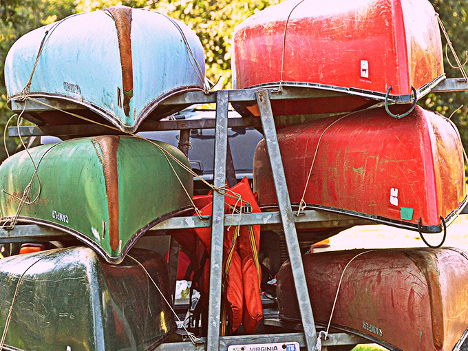 A rainbow of canoes stacked like delicious layers in a vacation cake. Each vessel promises adventures waiting to be unwrapped.