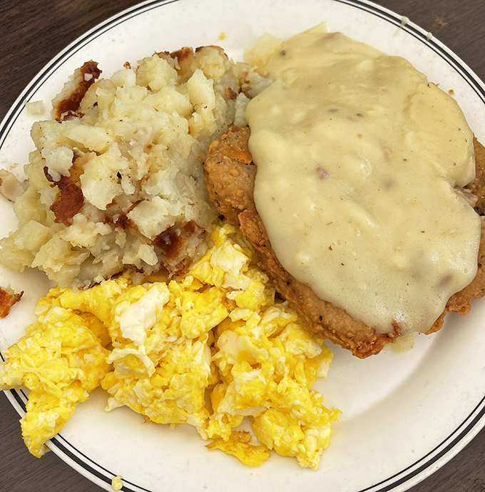 The holy trinity of diner perfection: golden scrambled eggs, crispy home fries, and country fried steak smothered in peppery gravy.