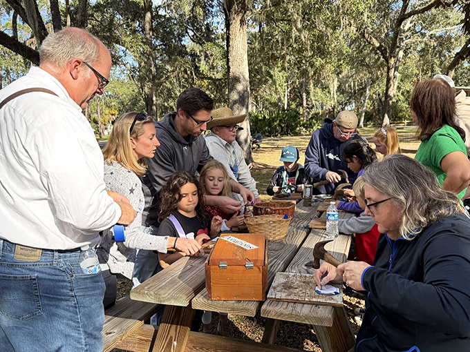 Gathered around picnic tables under a canopy of Spanish moss, families connect with history through interactive demonstrations and crafts.