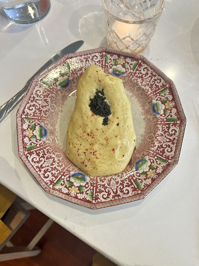 A delicate crepe cake arrives on vintage china, topped with what appears to be caviar—humble ingredients transformed into luxury.