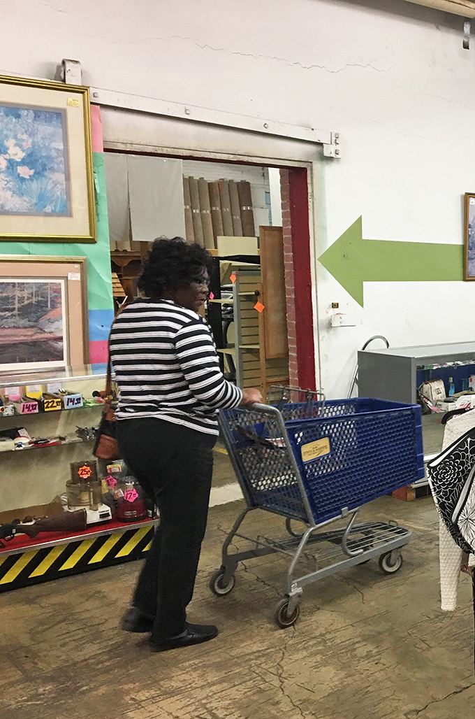 A shopper navigates the aisles with the blue cart of possibility – the universal symbol of thrift store commitment.