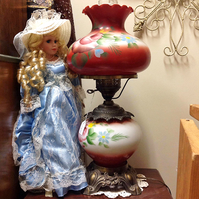 This porcelain doll in blue satin stands sentinel beside a hand-painted lamp—two relics from an era when craftsmanship outranked convenience.