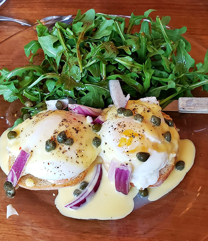 Eggs Benedict reimagined with vibrant red onions and capers. The hollandaise cascades down like a yellow waterfall of breakfast dreams.