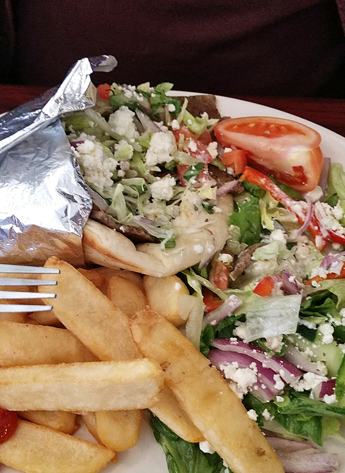 The Greek salad arrives like a Mediterranean vacation on a plate, with feta crumbles playing hide-and-seek among crisp vegetables and golden fries.