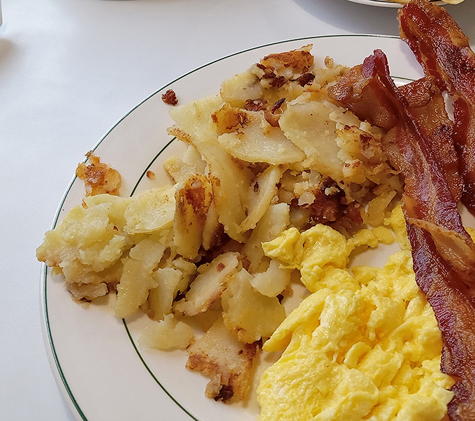 Crispy-edged home fries sharing a plate with fluffy scrambled eggs and bacon that's achieved that mythical balance between crisp and chewy. Breakfast nirvana exists, and it's right here.