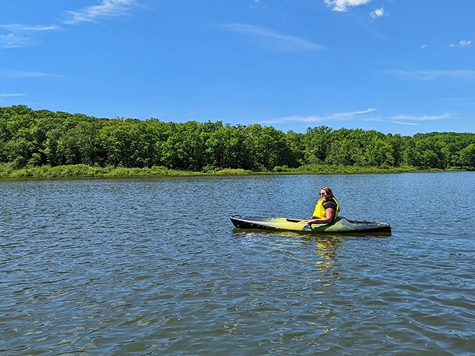 A solitary kayaker glides across mirror-like waters, creating the kind of peaceful moment that Instagram filters desperately try to replicate but never quite capture.