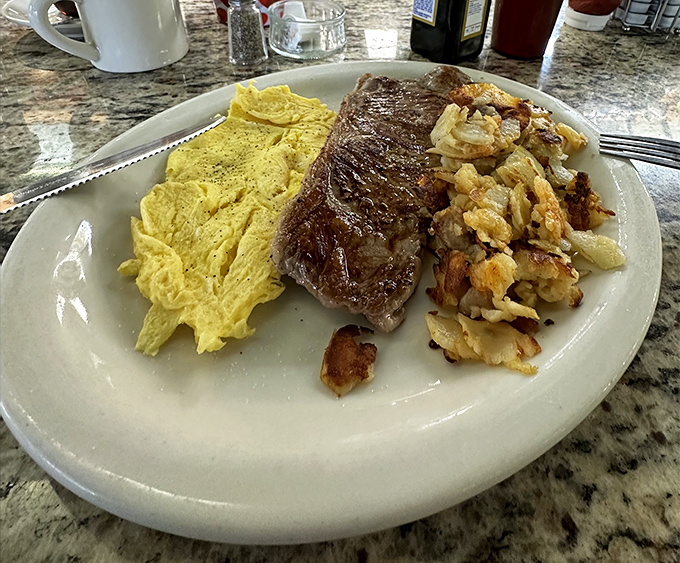 The holy trinity of breakfast: perfectly cooked steak, fluffy scrambled eggs, and home fries that strike the ideal balance between crispy and tender.