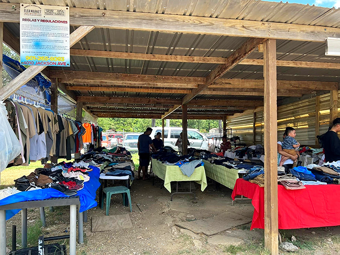 Under a rustic wooden shelter at the Memphis International Flea Market, rows of tables overflow with bargain clothing while shoppers browse in the shade.