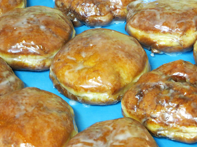 Apple fritters glistening with glaze that captures light like edible stained glass. Each one contains enough deliciousness to power a small town through a tough morning.