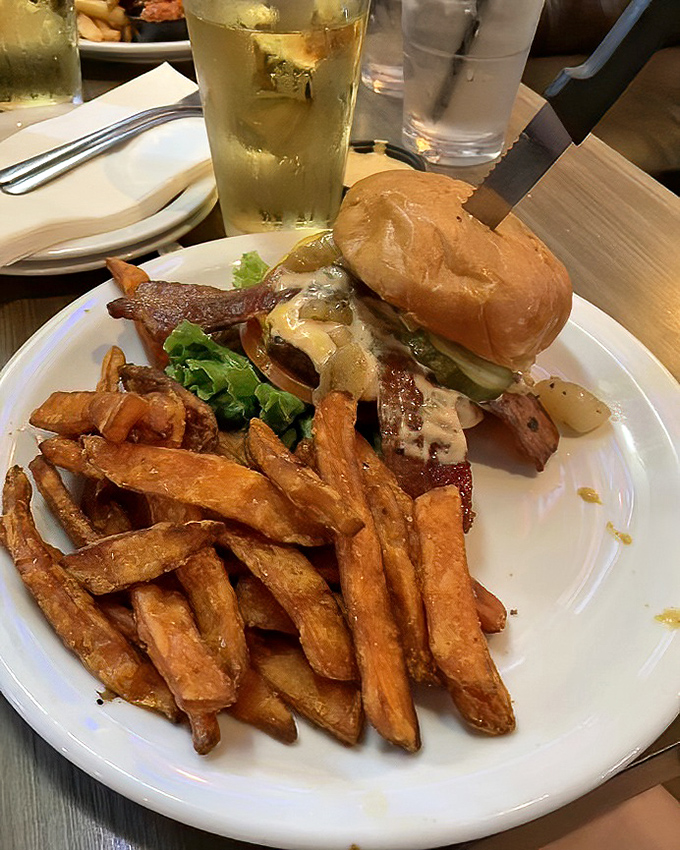 Sweet potato fries standing guard beside a burger that's practically winking at you. The beer in the background is just being a good wingman.
