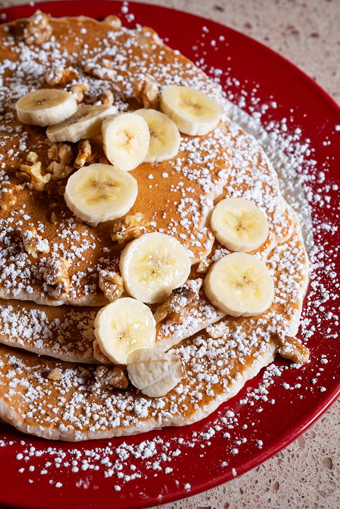 Banana nut pancakes stacked higher than your weekend expectations, dusted with powdered sugar that's basically breakfast confetti.