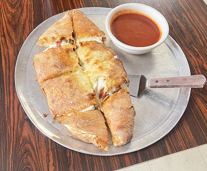 The calzone: pizza's mysterious, folded cousin. Golden-brown on the outside, molten cheese paradise on the inside, with that signature side of marinara.