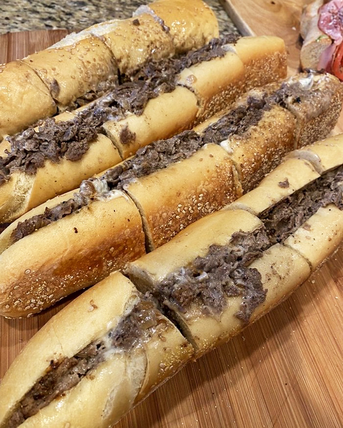 These cheesesteaks lined up like soldiers ready for delicious battle—sesame-seeded rolls cradling thinly sliced beef in perfect formation.