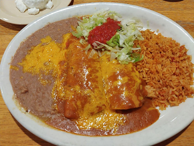 The holy trinity of Mexican comfort: enchiladas, beans, and rice. That sauce isn't just poured—it's lovingly blanketed over each enchilada like a mother tucking in her children.