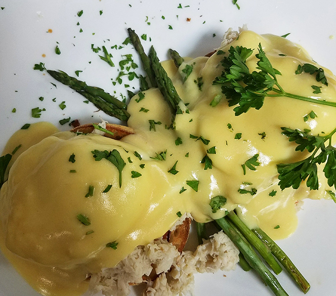 Hollandaise sauce cascading over asparagus like a yellow waterfall of buttery goodness. This eggs benedict isn't just breakfast&mdash;it's an event.