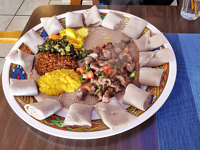 The fish goulash arrives like an edible painting—tender fish and vibrant vegetables arranged on injera canvas, ready for your hands to become the utensils.