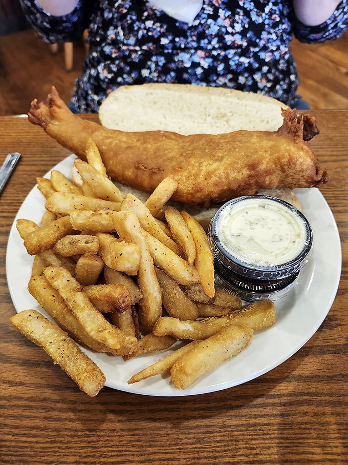 This fish sandwich towers with pride, featuring perfectly golden battered fish and crispy fries alongside.