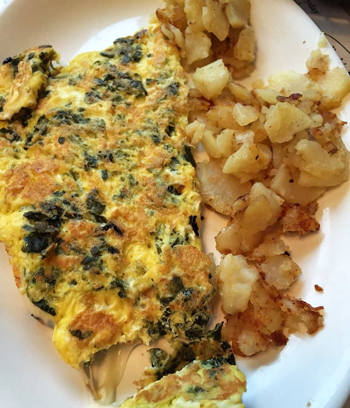 The Florentine omelet, a fluffy golden canvas painted with vibrant spinach, paired with home fries that could make a potato farmer weep with joy.