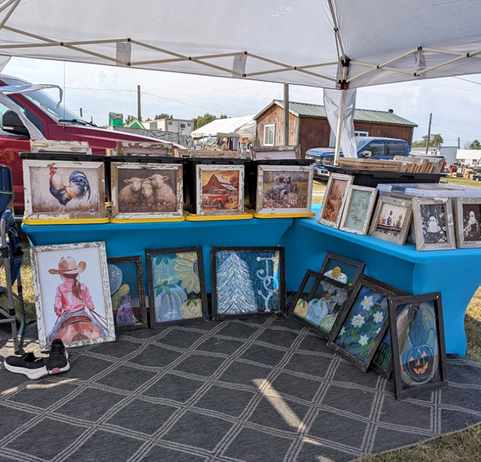 Art for every taste lines this booth's blue display wall&mdash;from roosters to cowgirls, these framed treasures await walls that need a touch of rural charm.